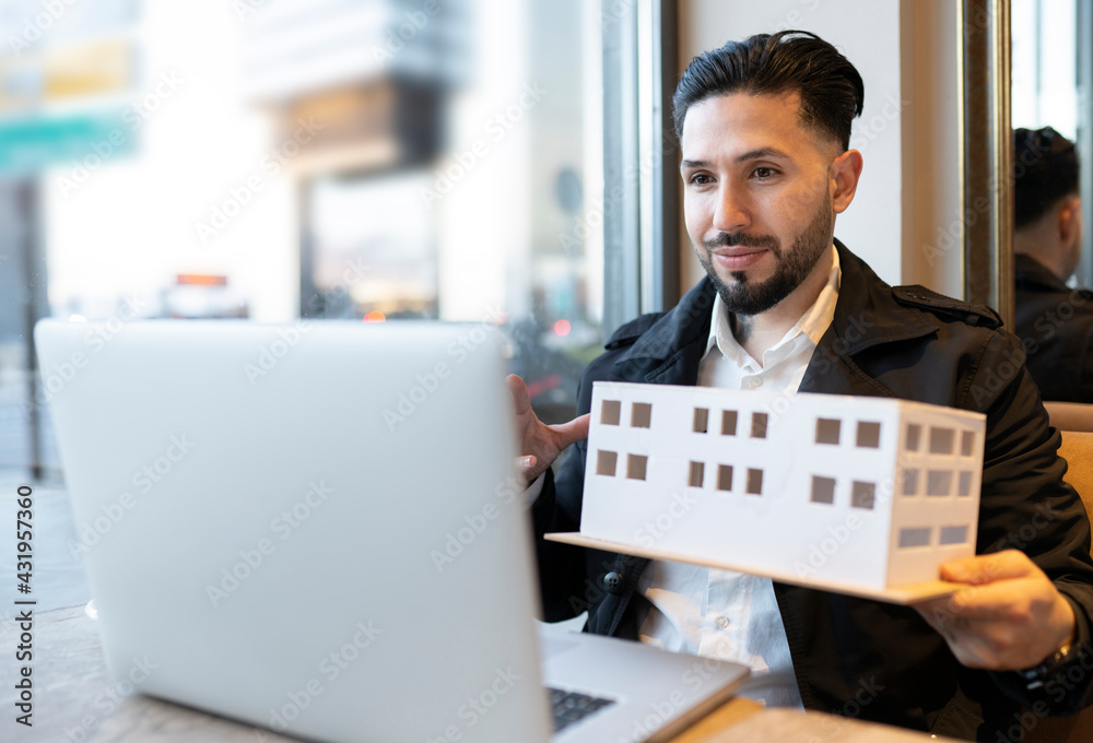Young male architect showing architectural model during video call ...