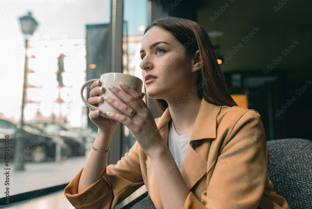 Beautiful woman drinking coffee while looking through window at cafe ...