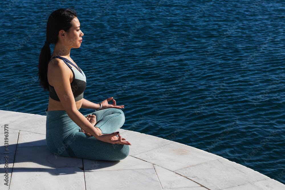 Female athlete practicing lotus position on promenade during sunny day ...