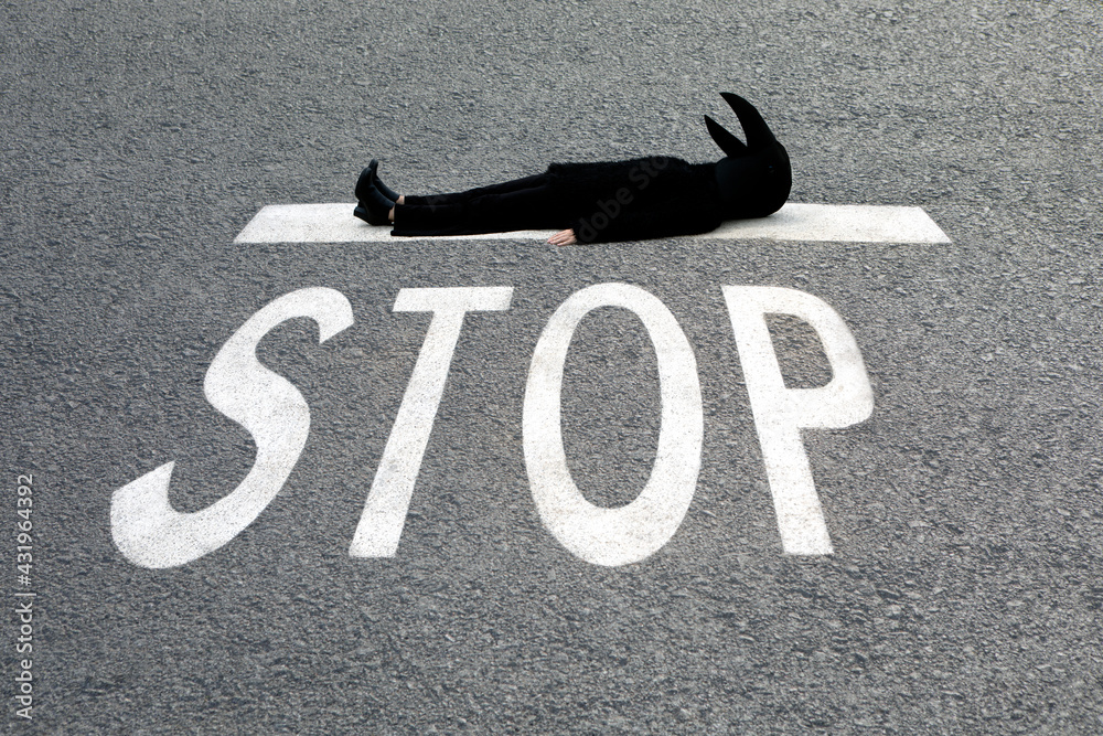 Female in crow costume lying down at STOP sign on road Stock Photo ...