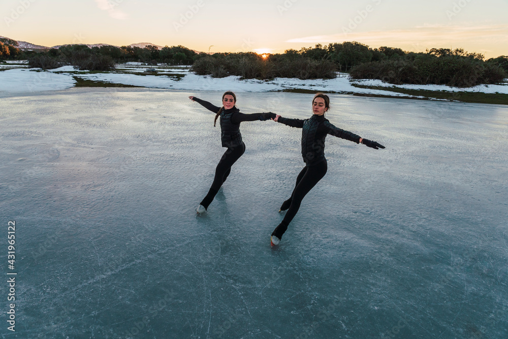 Two female figure skaters practicing together on frozen lake at dusk ...