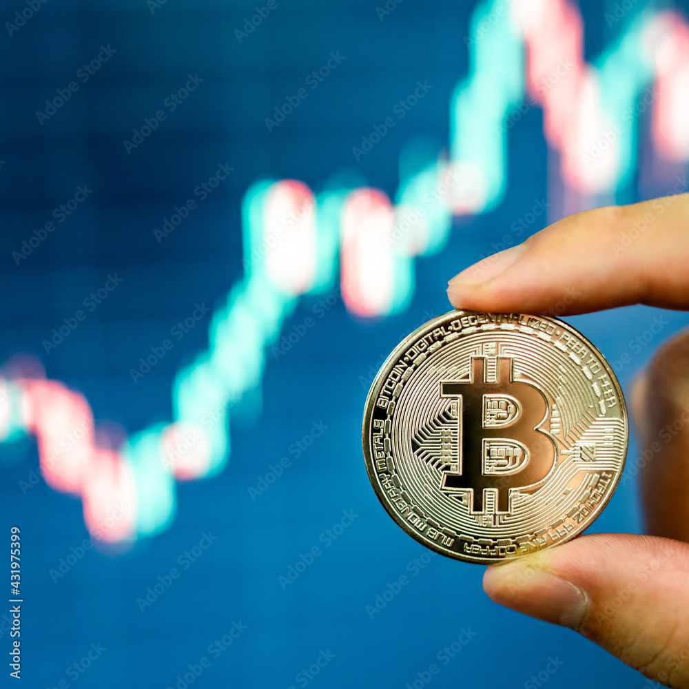 Investor hand holding silver Bitcoin with blurred candlestick chart in ...