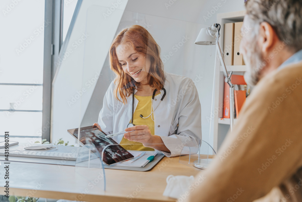Smiling doctor explaining patient over x-ray while sitting by screen ...
