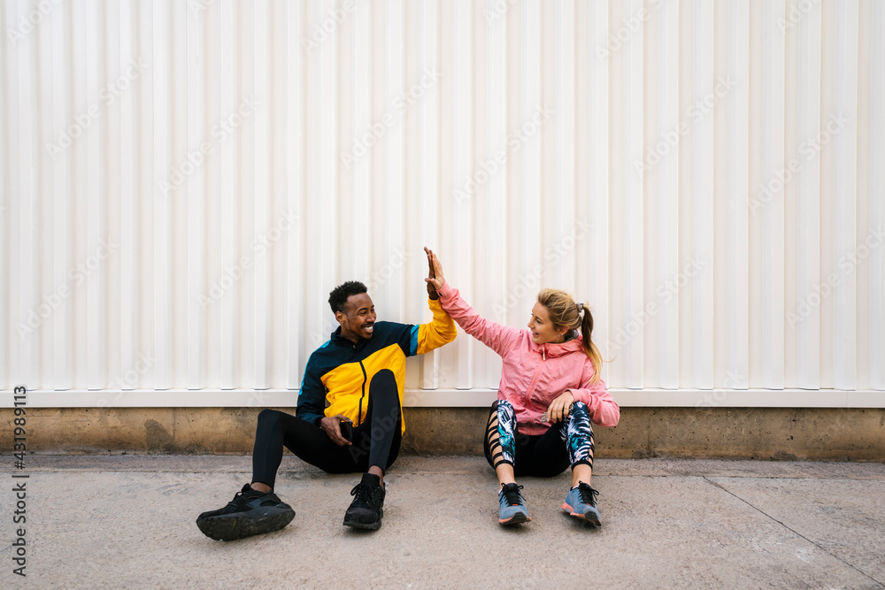 Male and female athlete doing high-five while sitting on sidewalk ...