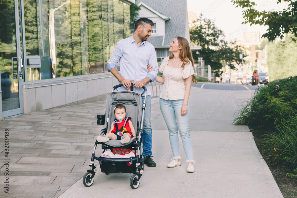 Caucasian mother and father walking with baby daughter in stroller ...
