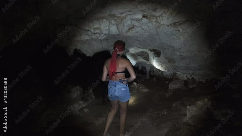 Woman explores the stalactites inside a dark deep cave, illuminating ...