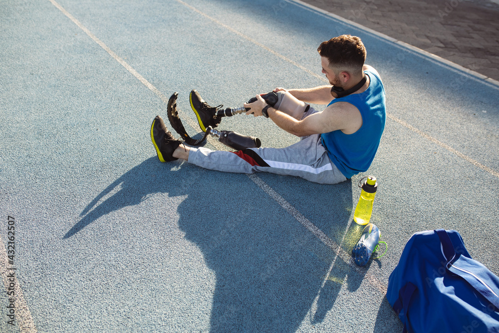 Caucasian male athlete fixing his prosthetic leg while sitting on ...