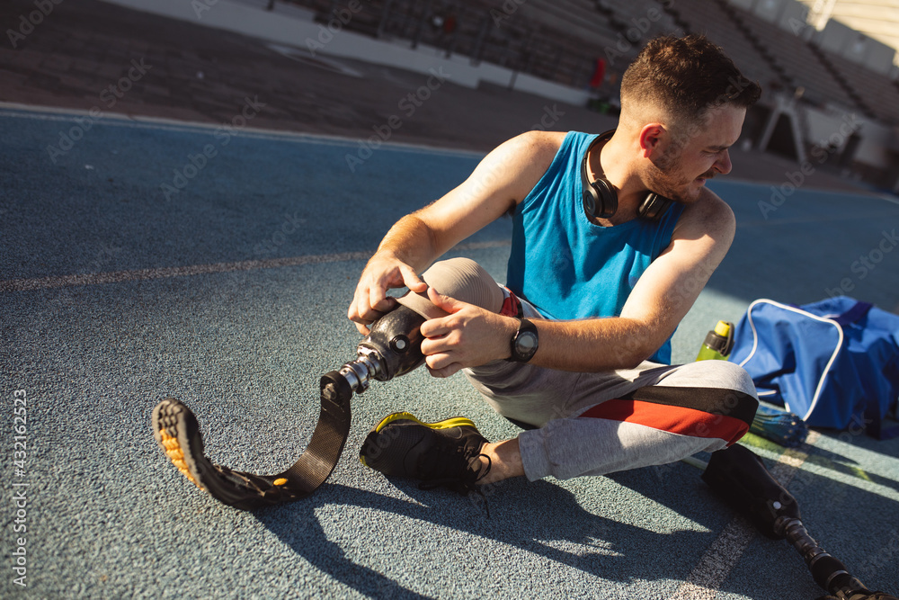 Caucasian male athlete fixing his prosthetic leg while sitting on ...