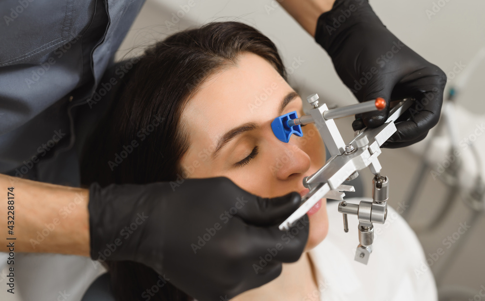An experienced dentist placing a facial bow for woman patient to ...