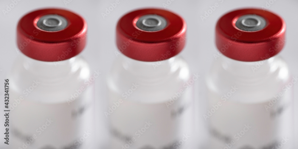 Row with three vaccine vials with red cap on a light background. Liquid ...