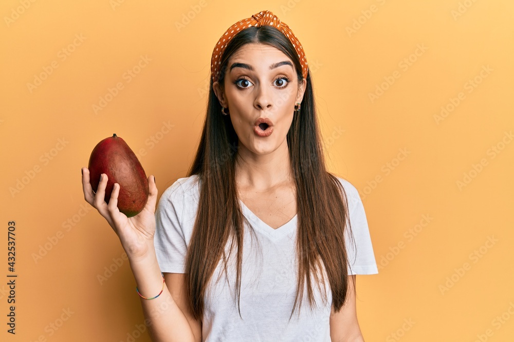 Beautiful brunette young woman holding mango scared and amazed with ...