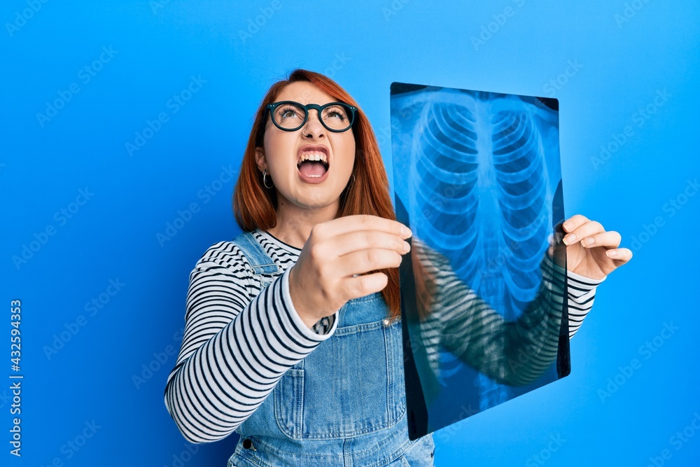 Beautiful redhead woman holding chest radiography angry and mad ...