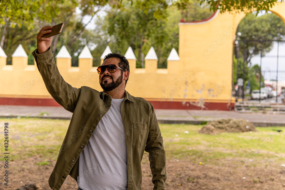 Young bearded happy mexican man wearing sunglasses and jacket taking a ...