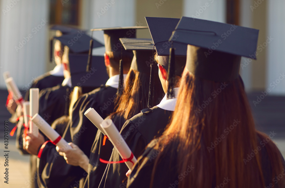 Rear view of university graduates crowd group line up holding degree ...