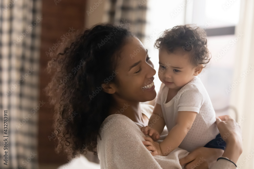 Smiling young African American mother play caress small toddler girl ...