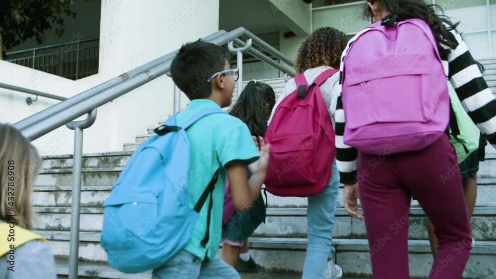 Multiethic group of schoolkids going up stairs. Older girls holding ...