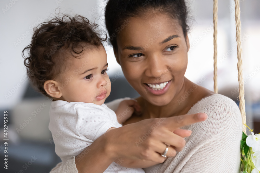 Close up of happy young African American mom hold cute little baby daughter play together at ...