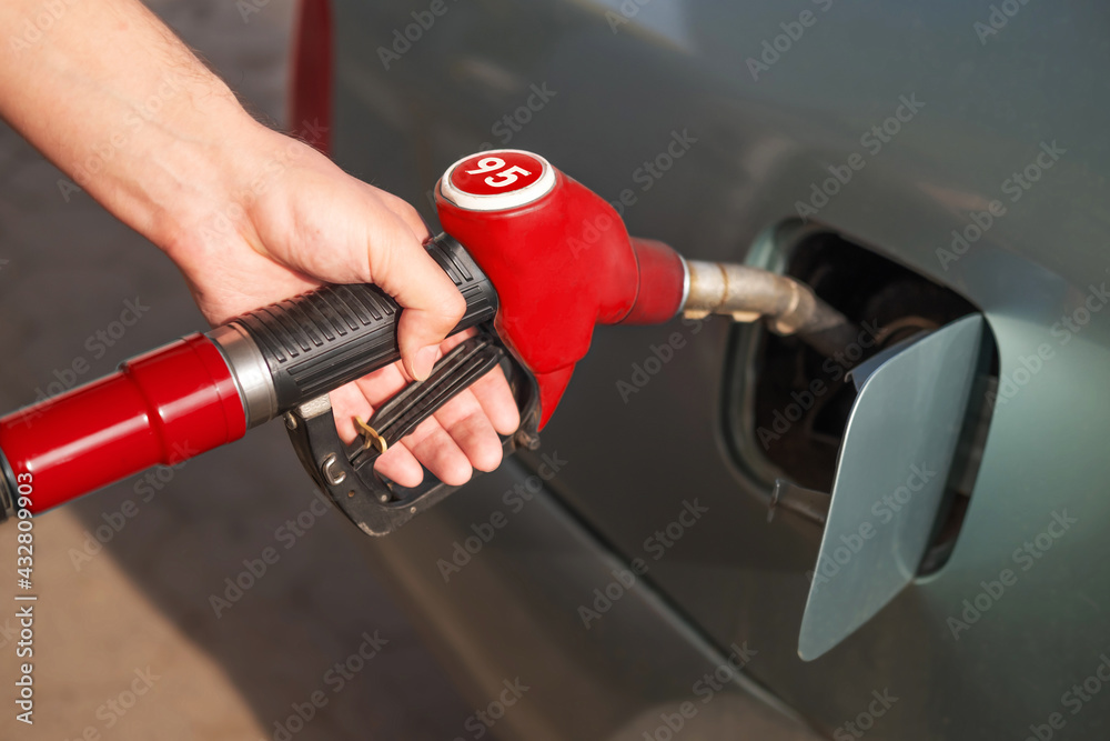Refueling the car with fuel. A red fuel nozzle is installed in the gas ...