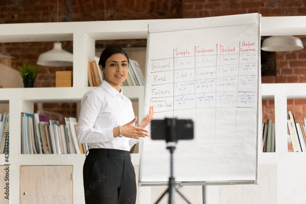 Smiling Indian young woman teacher recording flip chart presentation ...
