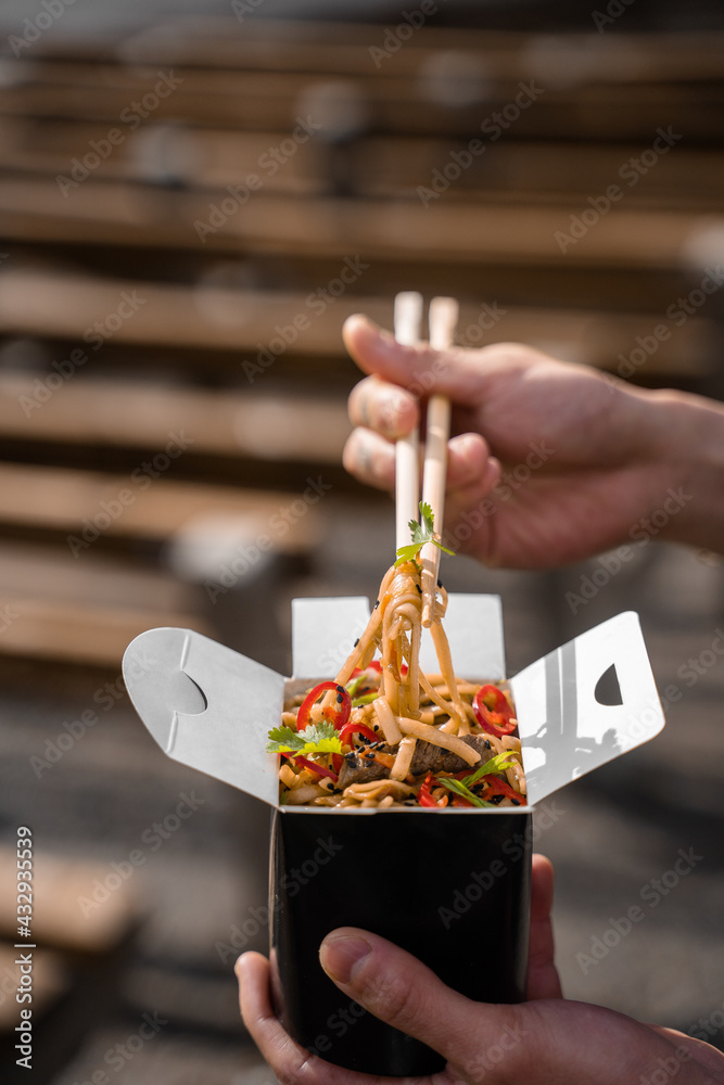 Wok in box in black food container. Holding spicy noodles with ...