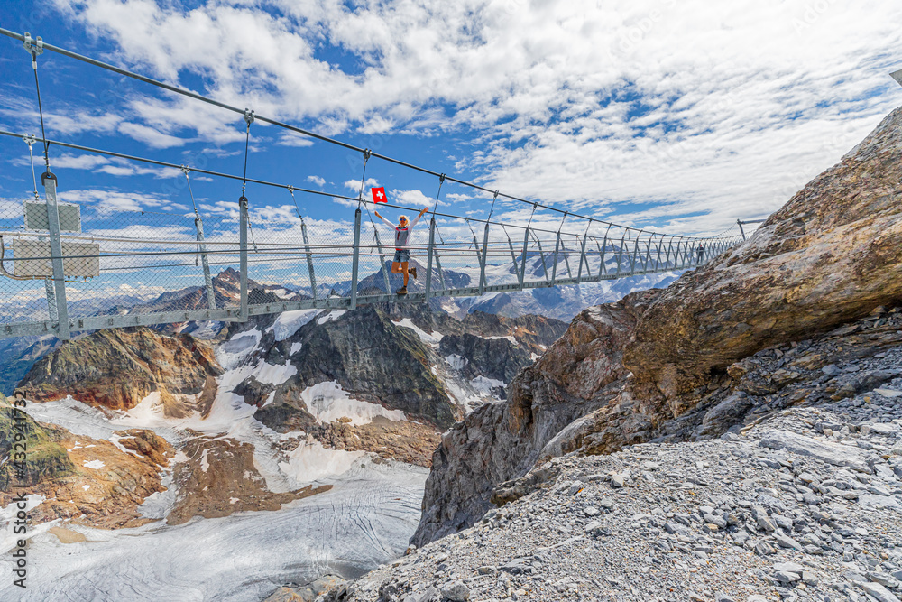 Woman on suspension bridge waving a Swiss flag. Titlis cliff walk with ...