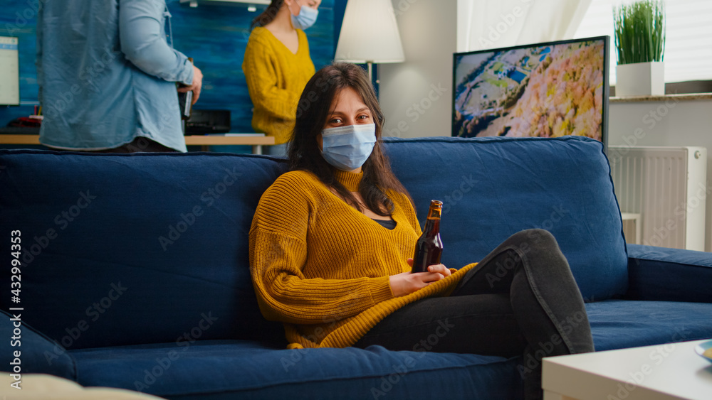 Woman relaxing with friends sitting on couch wearing face mask against ...