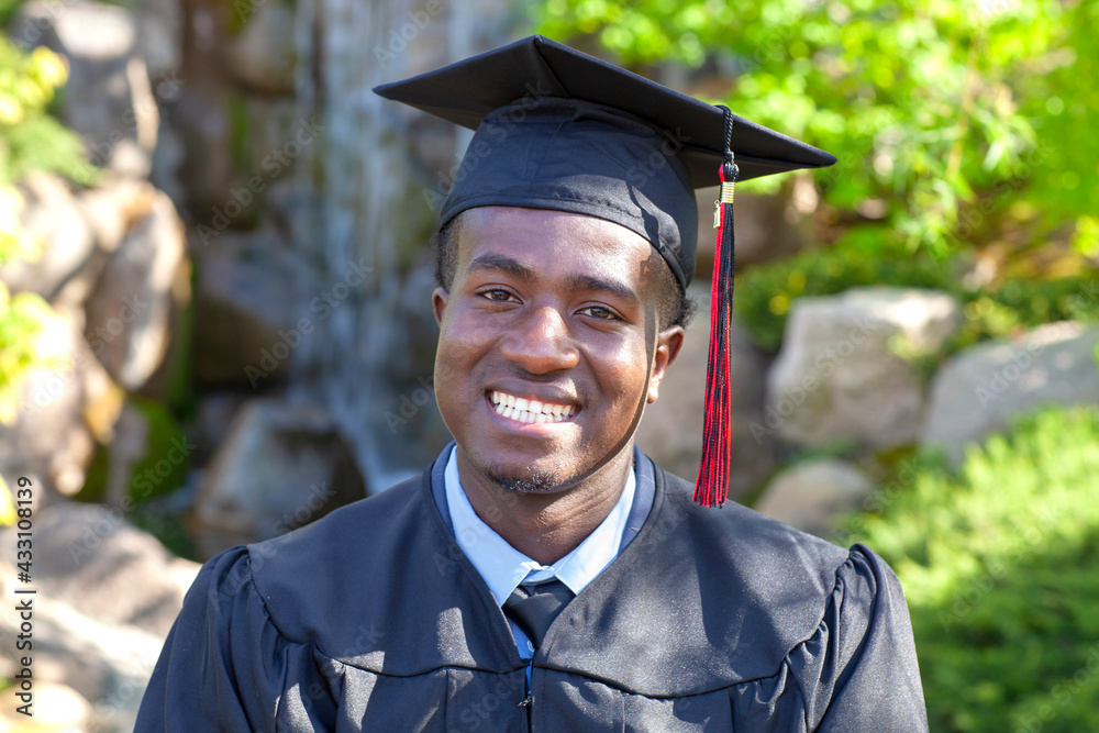 Handsome young black college graduate wearing cap and gown smiles ...