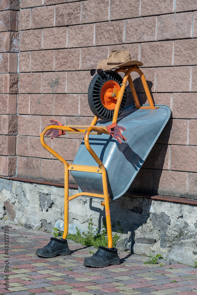 Old funny wheelbarrow of human form, leaning against a stone fence in a ...