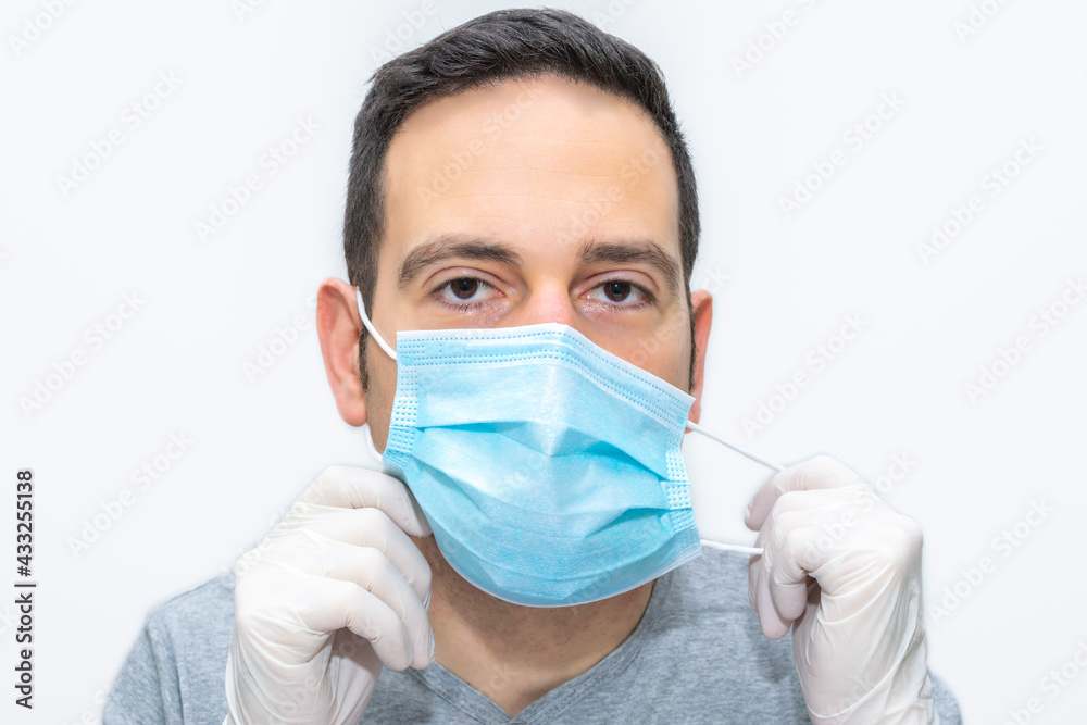 Close-up of a man removing his surgical mask with one hand on a white ...