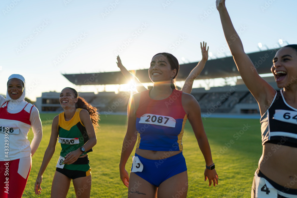 Happy female track and field athletes celebrating in sunny stadium ...