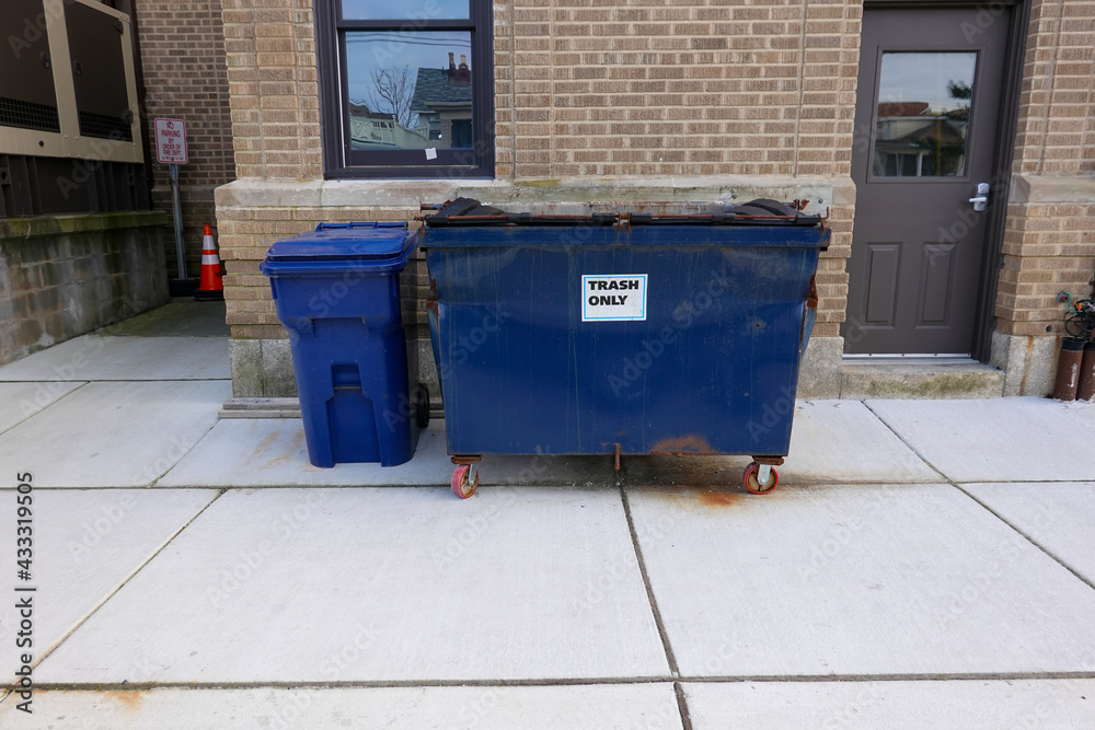 Foto de Small blue dented dumpster on wheels on a sidewalk next to a ...