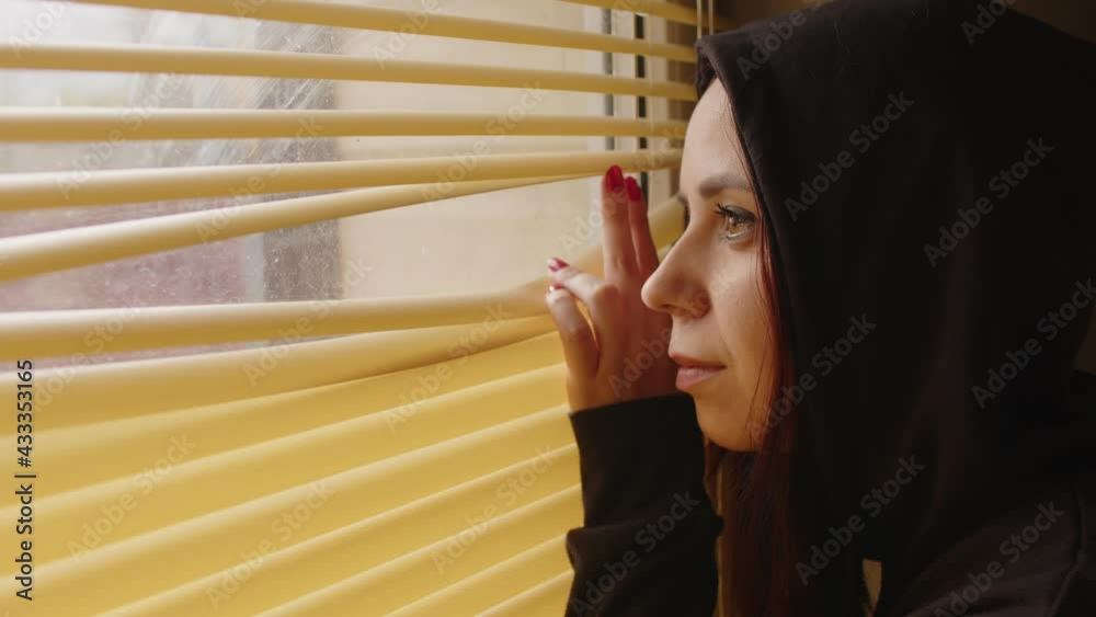 Close up of young woman watching through window blinds at home ...