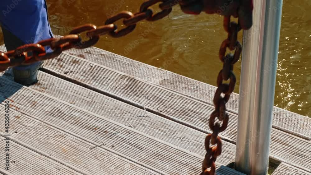 Legs of two men onboard of tug who put big chain into water to fix it ...