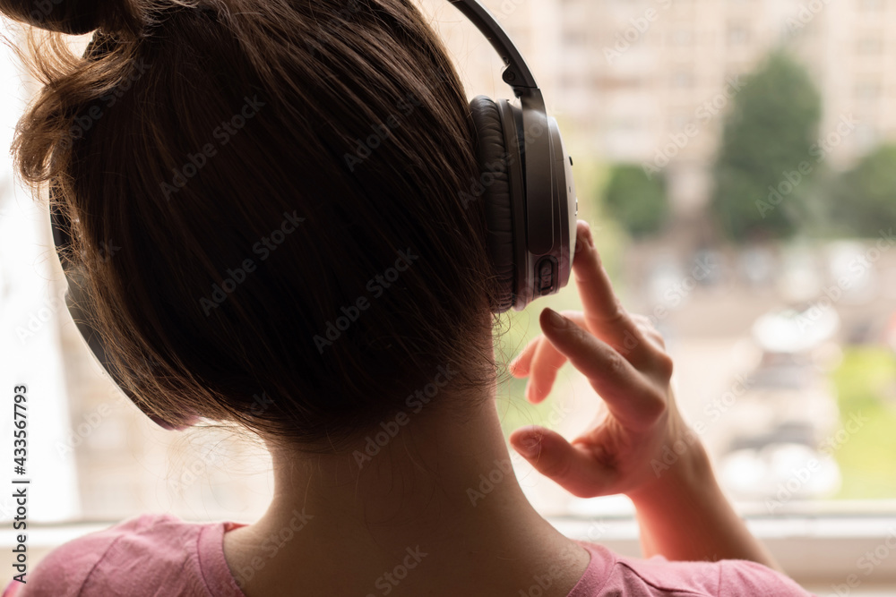 Back view of a lonely young woman listening to music with headphones ...