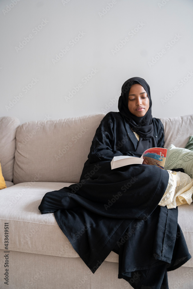Black Muslim teenage girl reading a book in the living room Stock Photo ...
