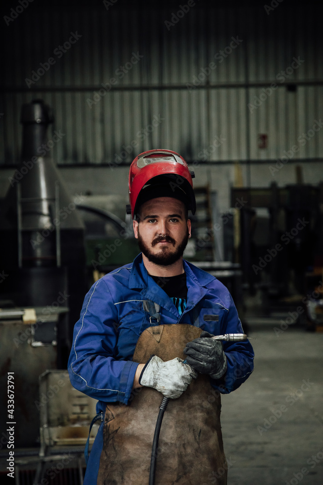 Mechanic in protective helmet and apron on blue overall standing with ...