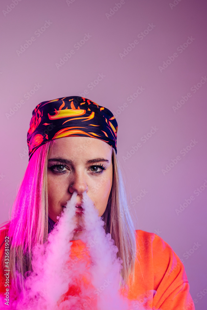 Cool female in street style outfit smoking e cigarette and exhaling ...