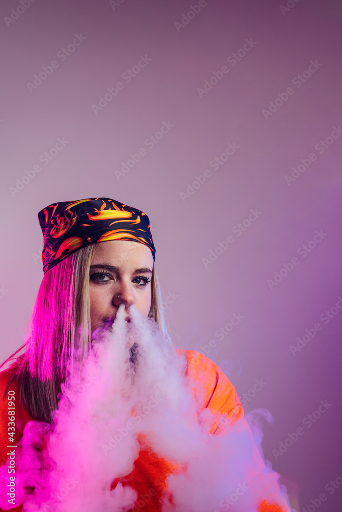 Cool female in street style outfit smoking e cigarette and exhaling ...
