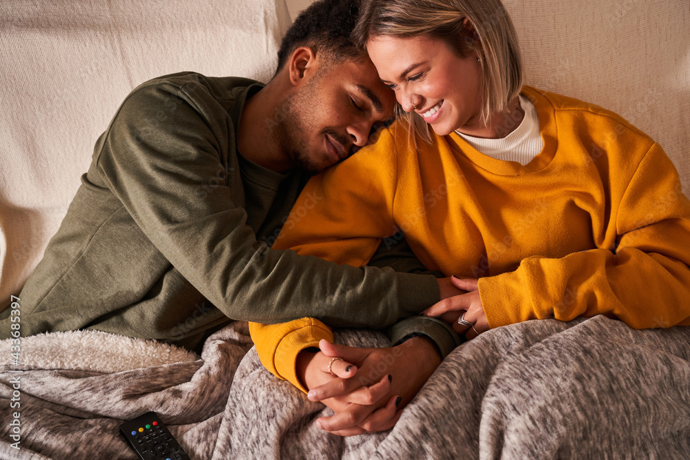 High angle of loving multiethnic couple relaxing on couch under blanket ...