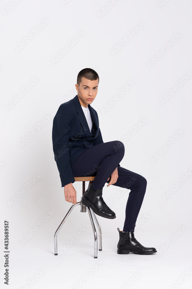 Side view of determined male wearing elegant suit sitting on stool on ...