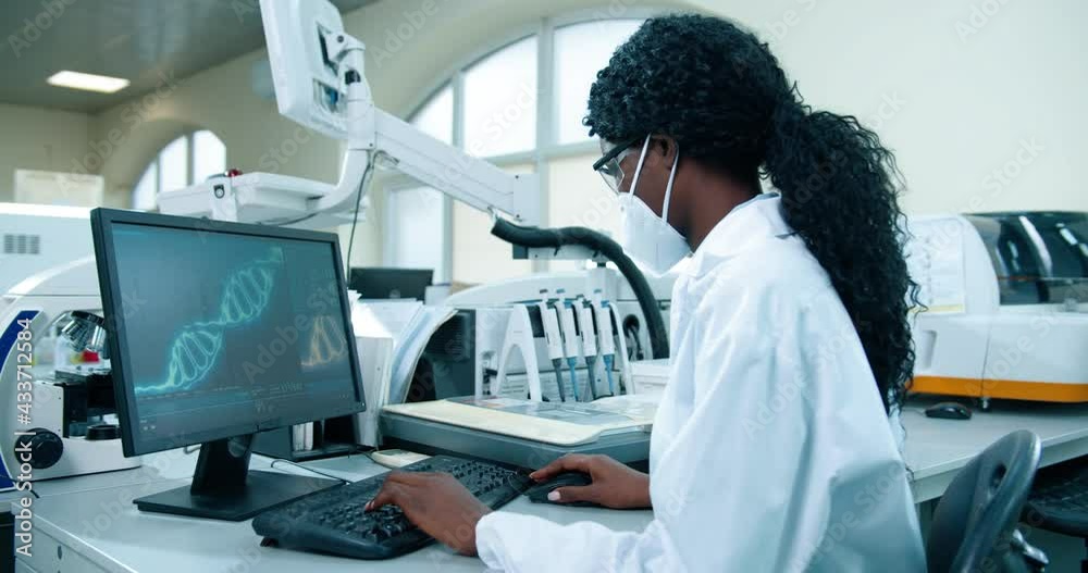 Side view of African American young female medical expert sitting at workplace in lab working ...