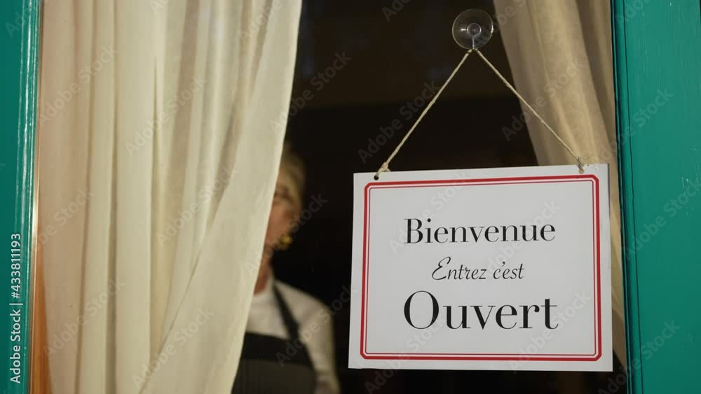 Female shop owner turning ouvert ferme sign on french cafe glass door ...