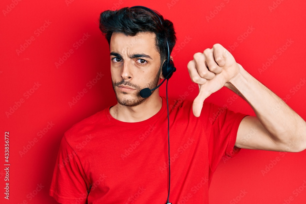 Young hispanic man wearing call center agent headset with angry face ...