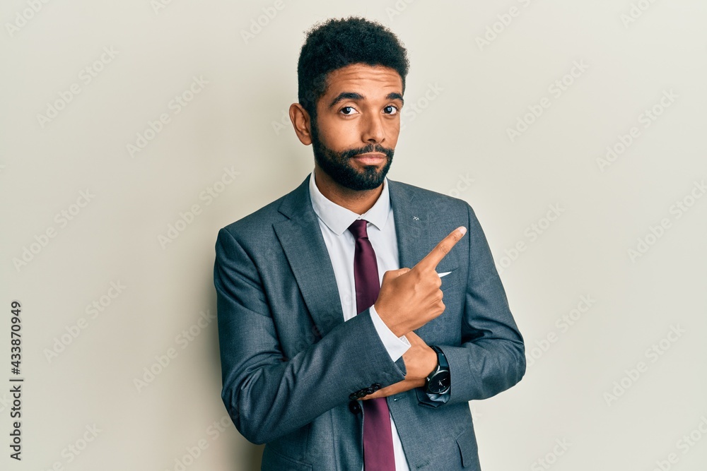 Handsome hispanic man with beard wearing business suit and tie pointing ...