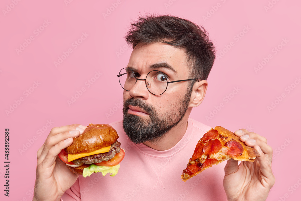 Eating junk food. Serious attentive bearded adult European man holds ...