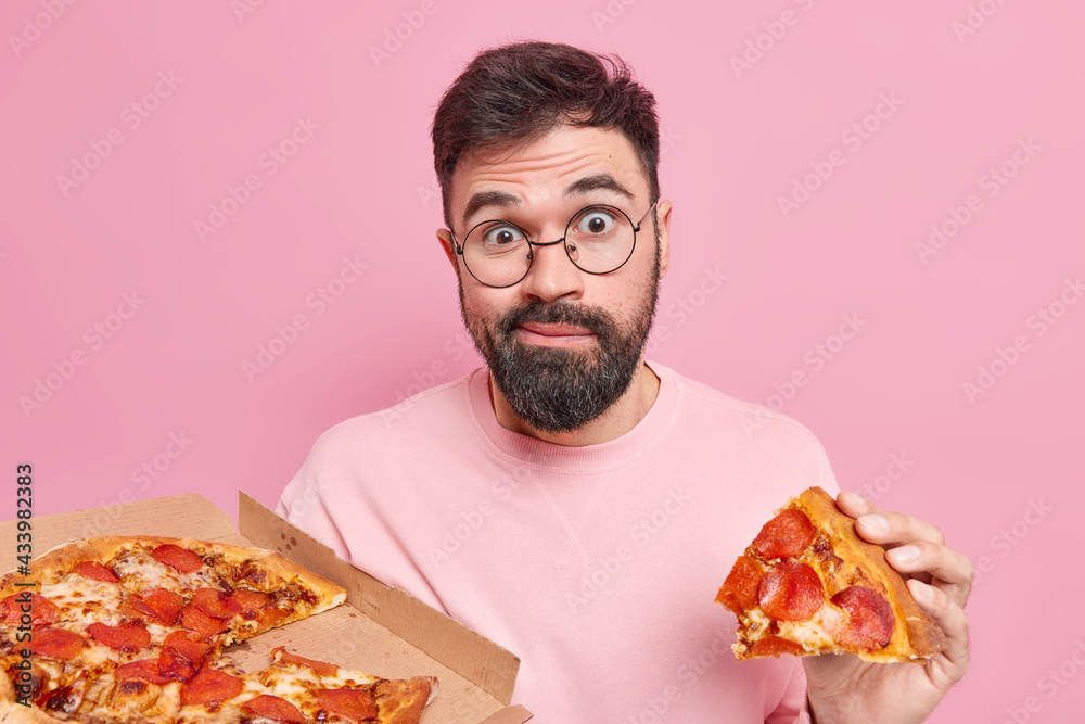 Confused surprised unshaven young man eats tasty pizza has fast food ...