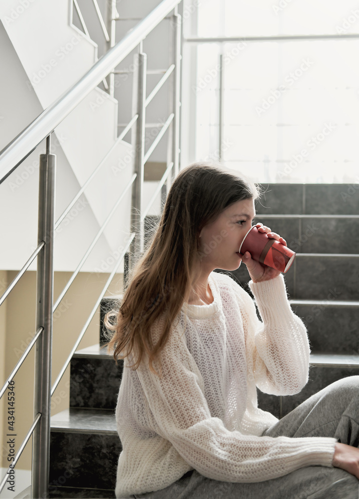 shcool teenage girl sitting on a staircase in a school and drinking ...