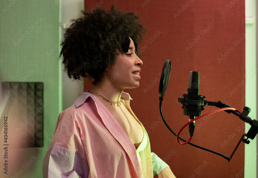 Black female singer performing song against microphone with pop filter ...