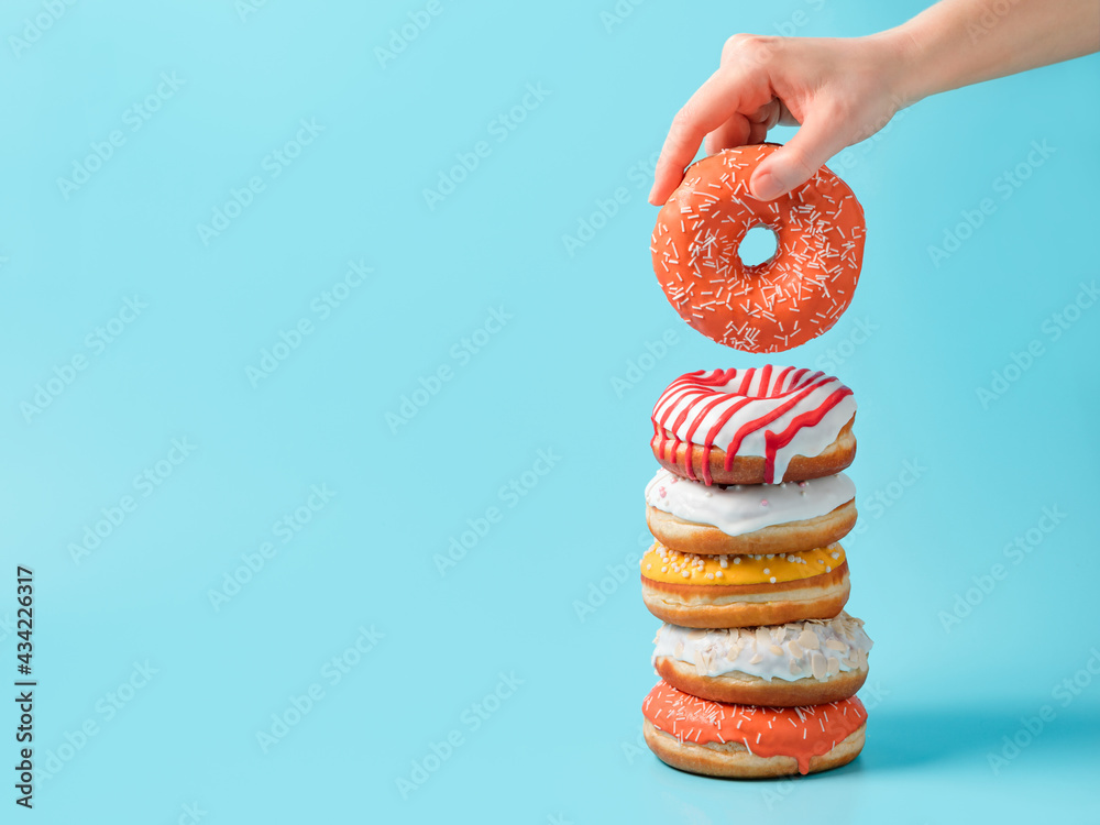 Stack of assorted donuts and one donut in female hand on blue ...
