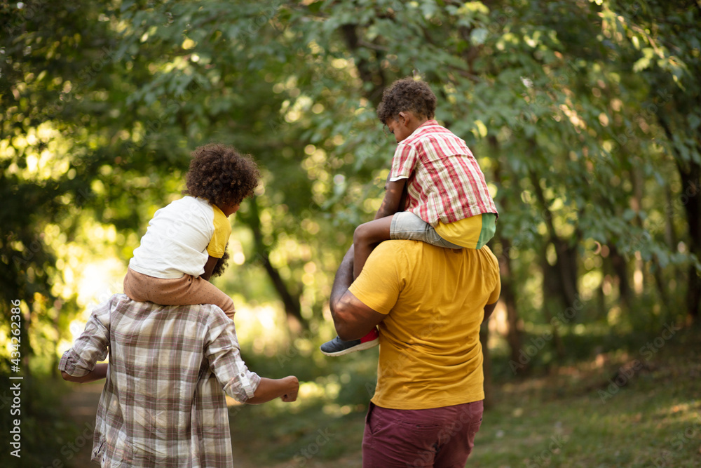 African American family walking trough park. Parents carrying children ...